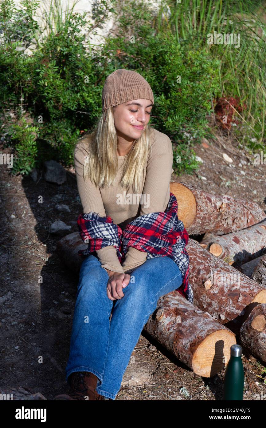 Smiling young woman with eyes closed sitting on wooden log Stock Photo ...