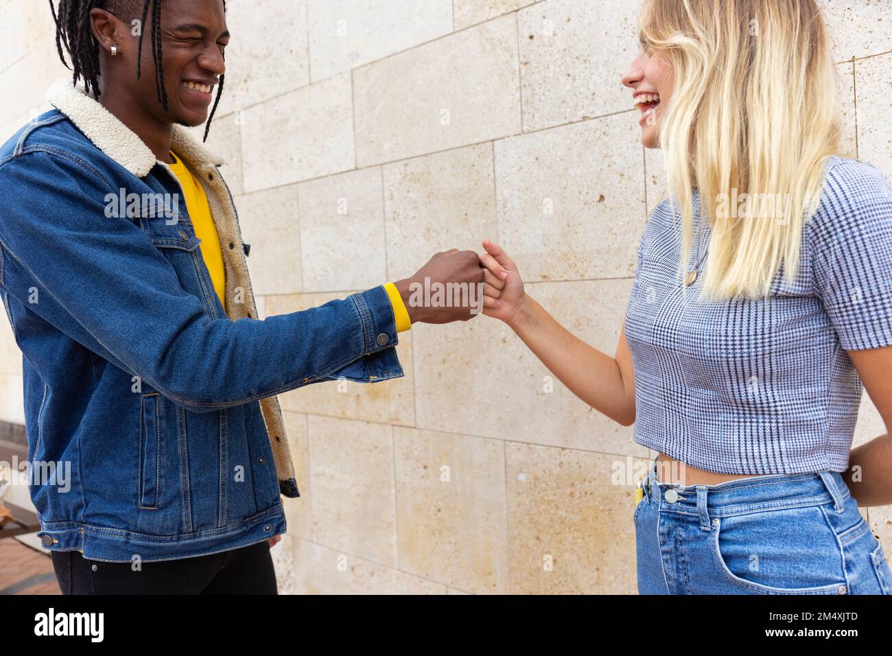 Friends giving fist bump together standing in front of wall Stock Photo ...