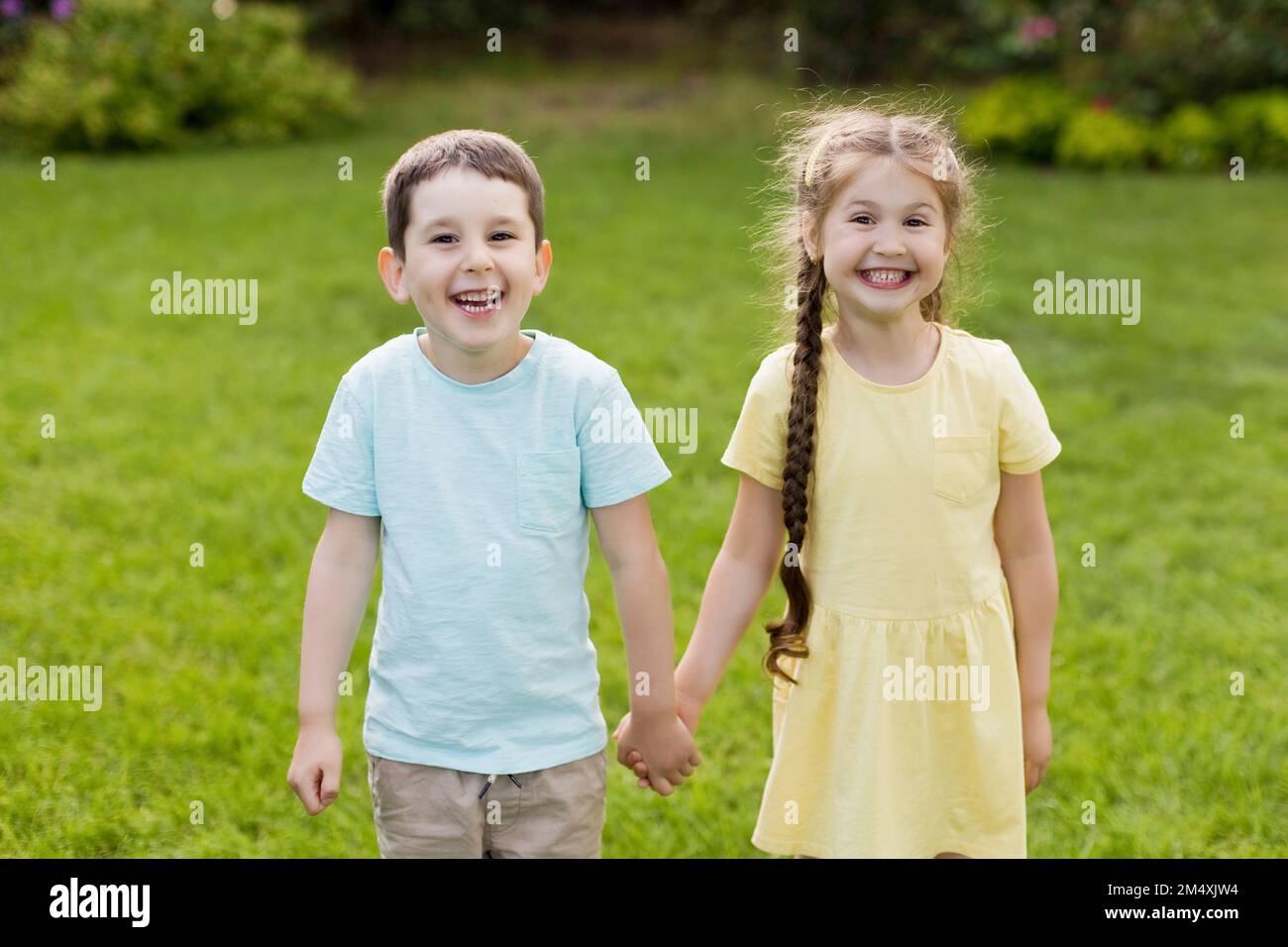 Cheerful brother and sister holding hands standing in garden Stock ...