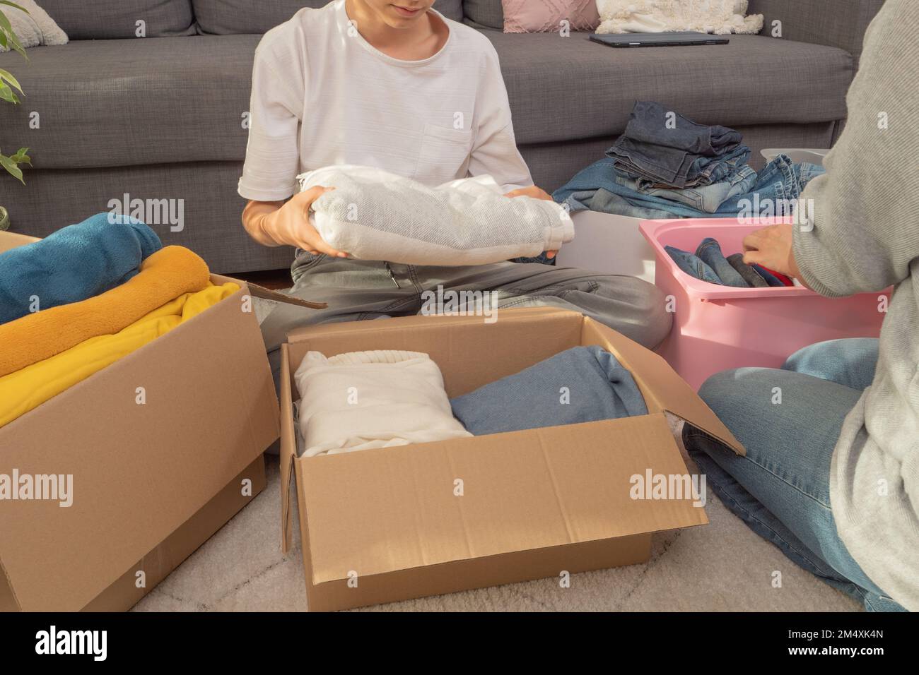 Woman and son sorting clothes and packing into cardboard box. Donations for charity, help low ...