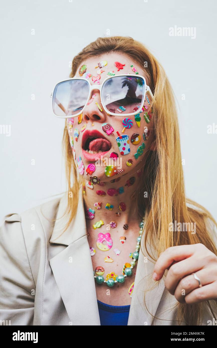 Woman with stickers on face wearing sunglasses in front of white ...