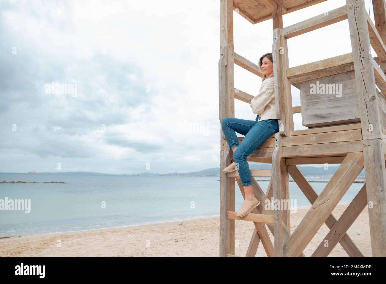 Smiling young woman sitting on wooden lifeguard hut at beach Stock ...