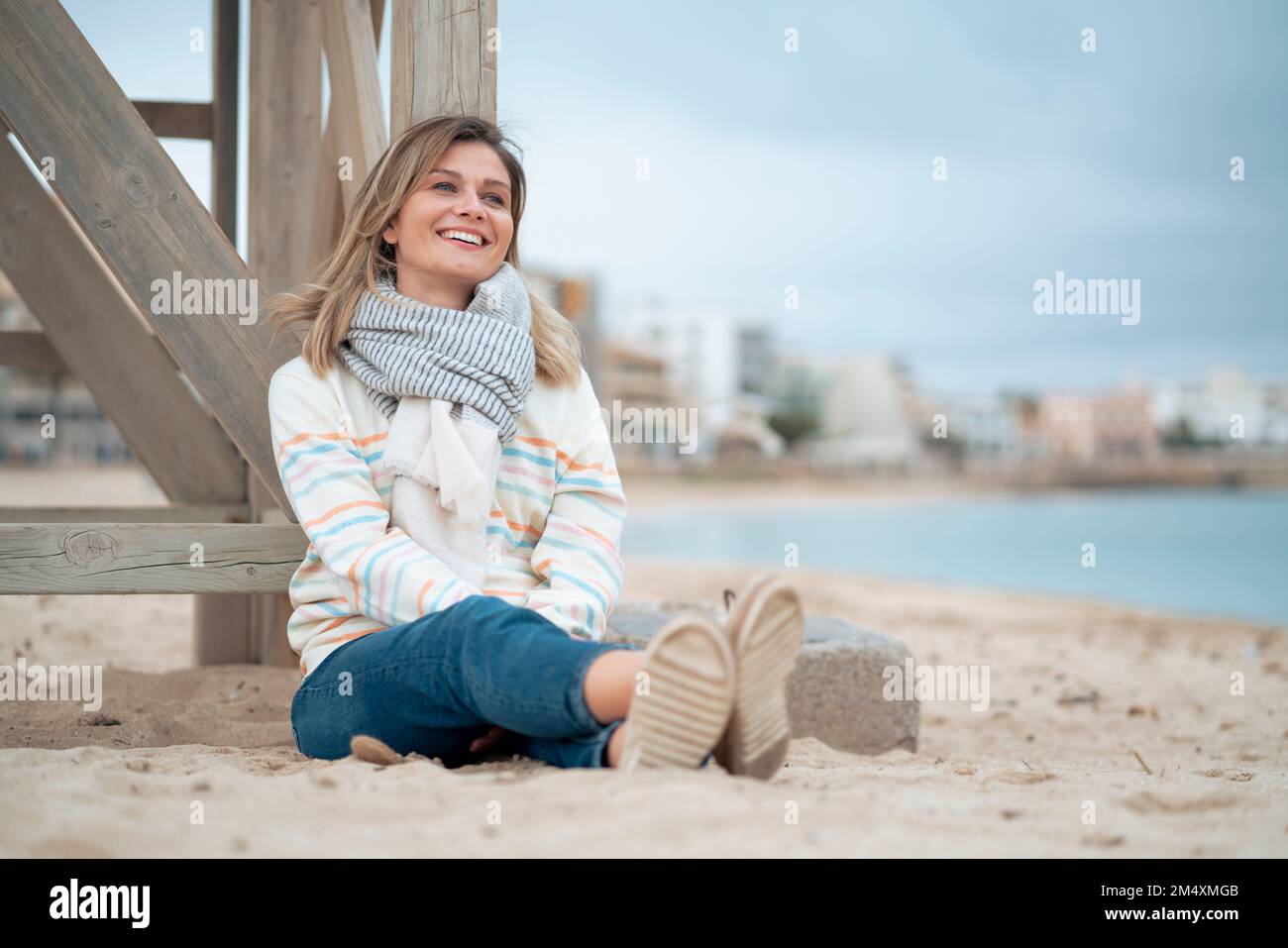 Smiling young woman leaning on wooden lifeguard hut day dreaming at ...