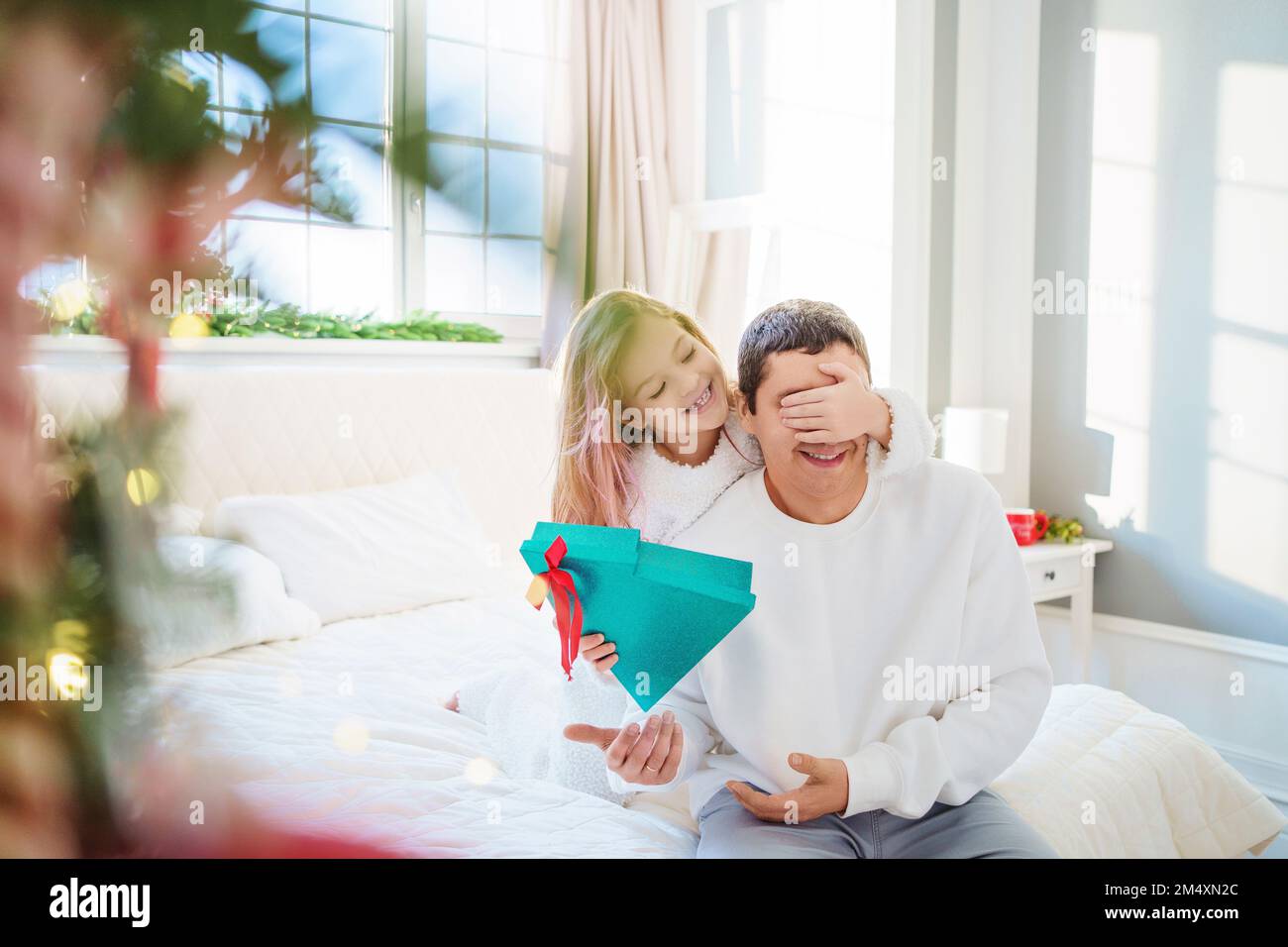 Happy girl giving surprise Christmas gift to father sitting on bed at ...