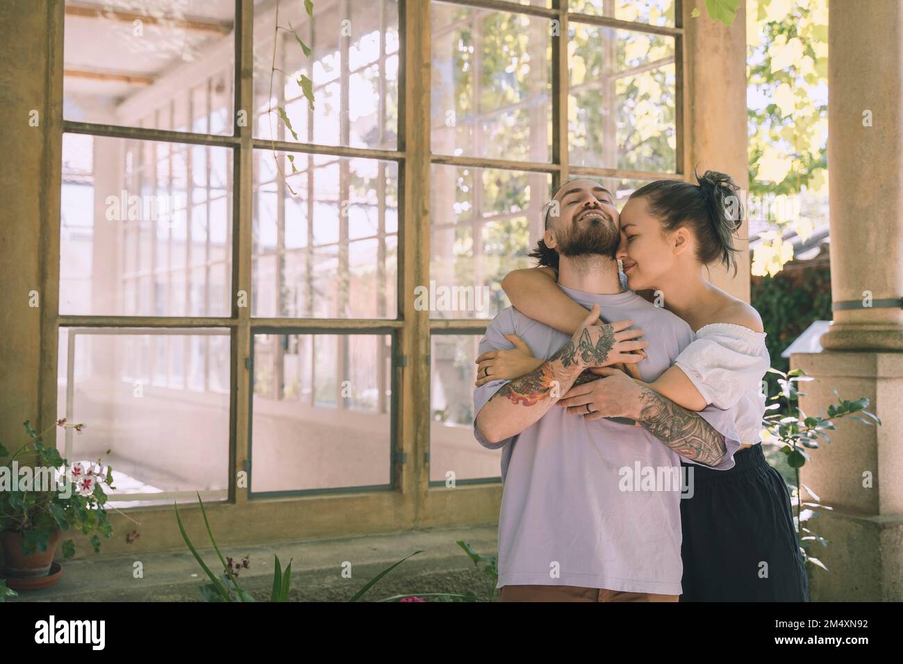 Affectionate woman embracing hipster boyfriend in front of window Stock ...