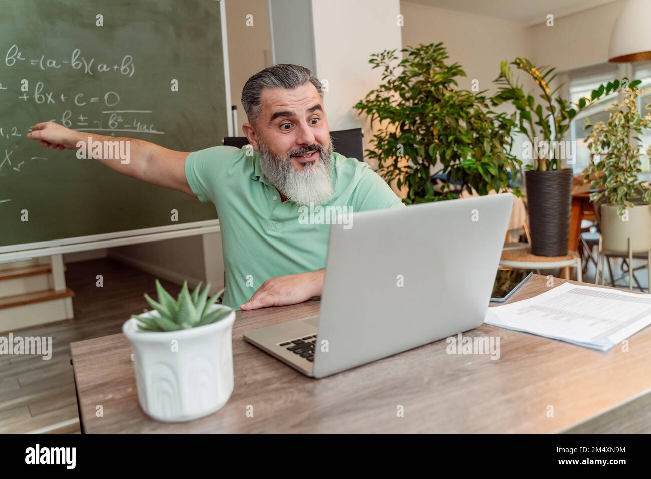 Teacher taking online lecture through video call on laptop at desk ...