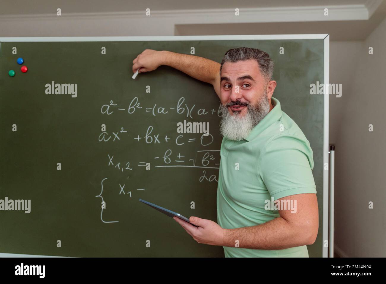 Teacher explaining mathematics on chalkboard holding tablet PC Stock ...