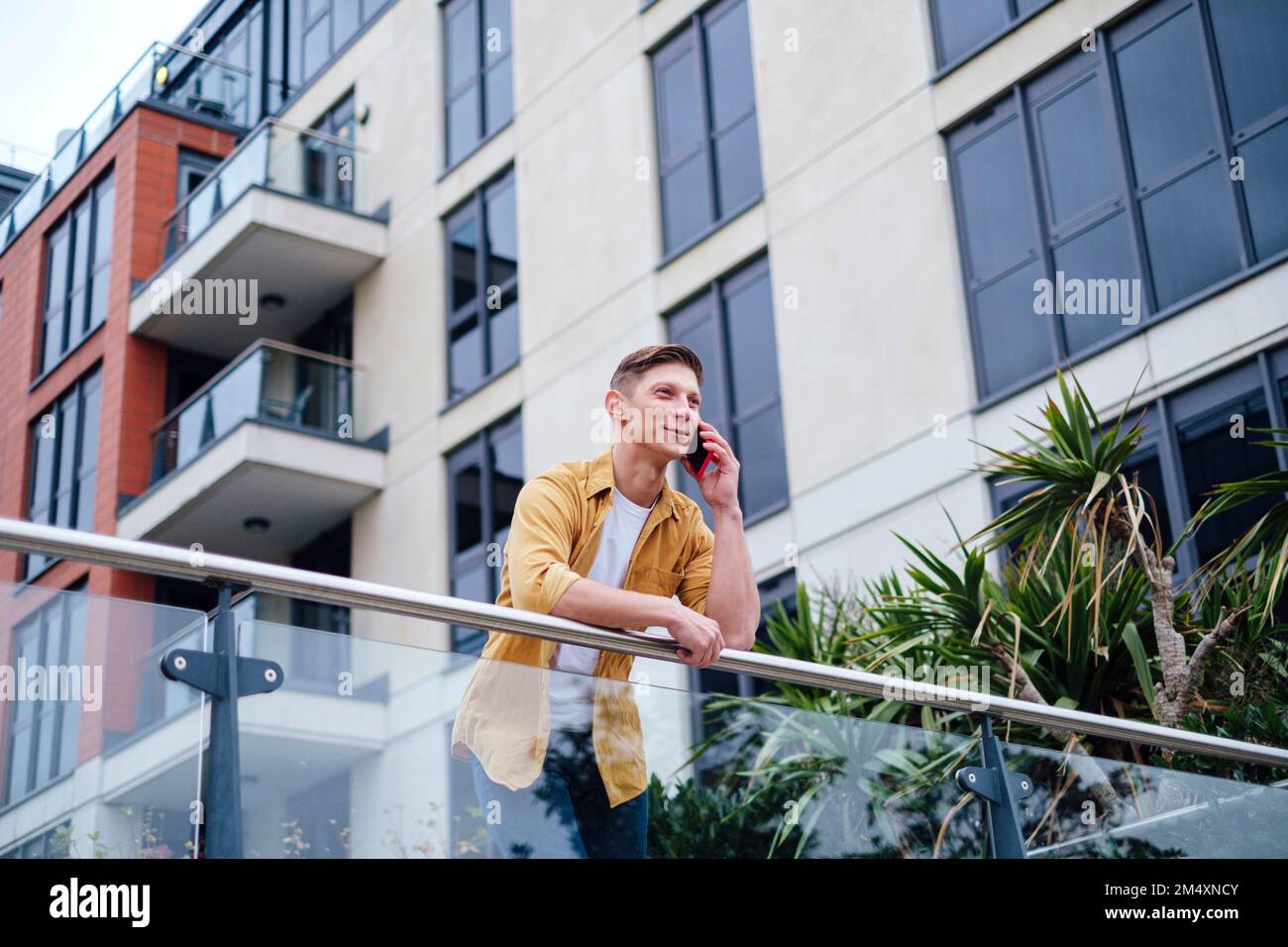 Smiling man talking through smart phone leaning on railing Stock Photo ...