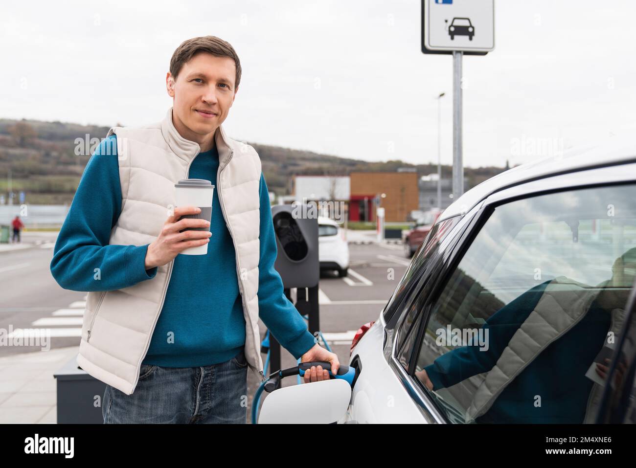 Man with disposable cup charging electric car at station Stock Photo ...