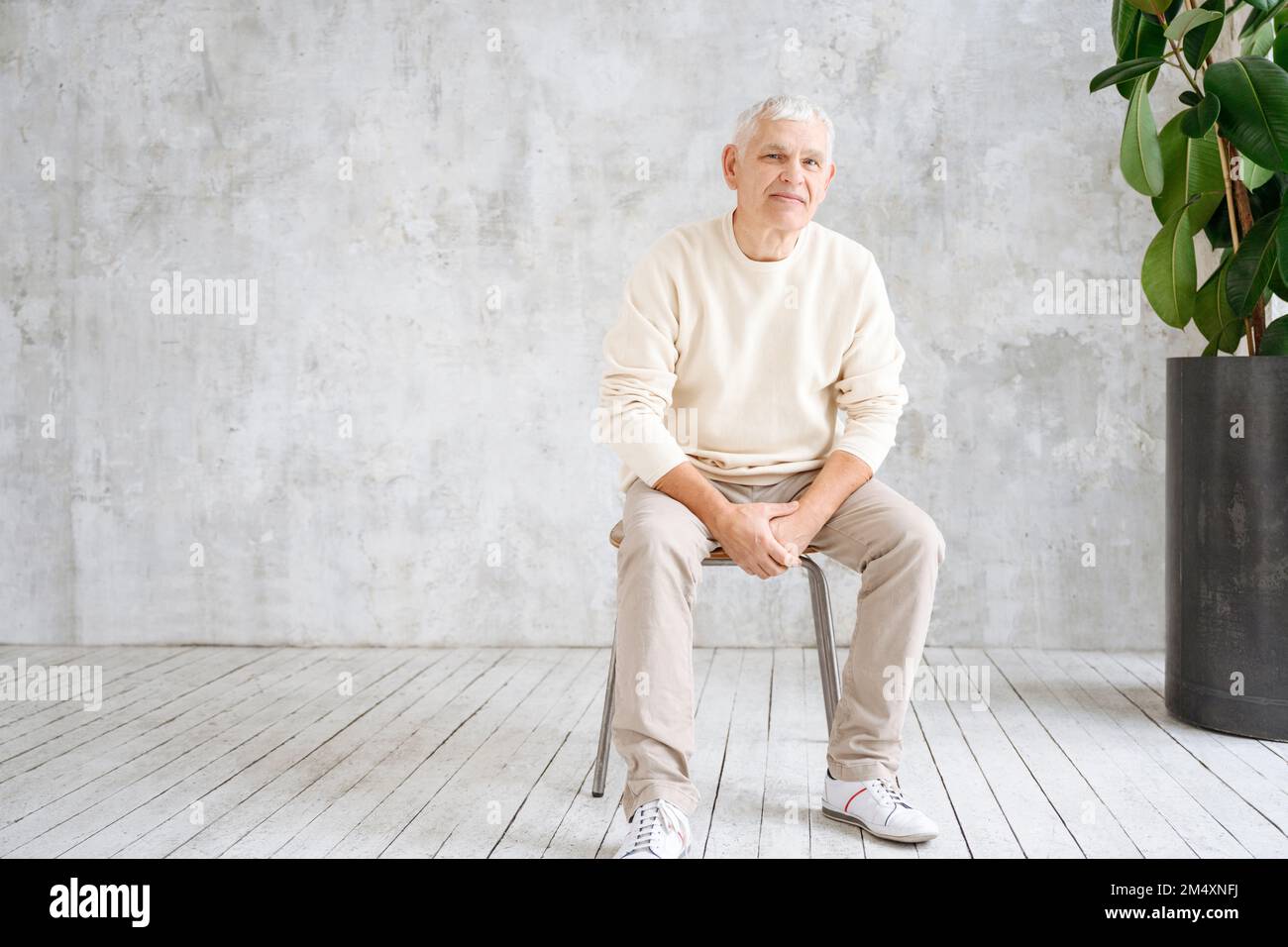 Senior man sitting on stool in front of wall Stock Photo - Alamy