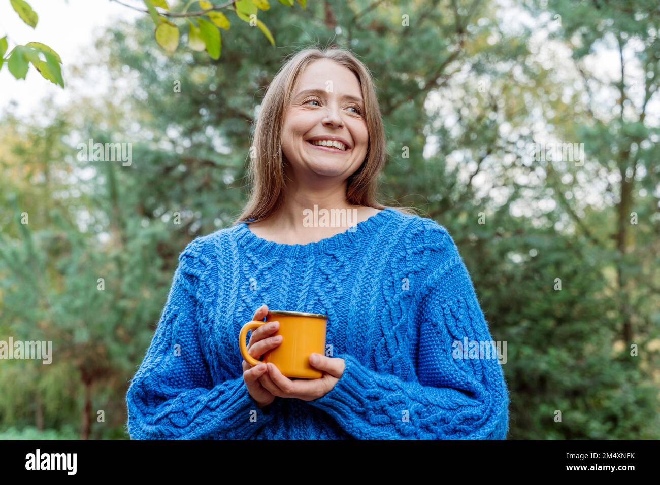 Smiling woman wearing blue sweater holding coffee cup day dreaming ...