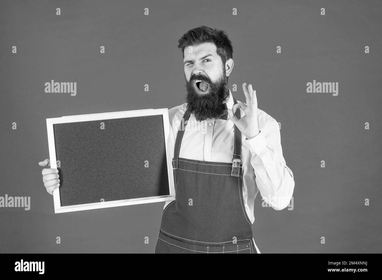 Happy winking man in barber apron hold school blackboard showing OK ...
