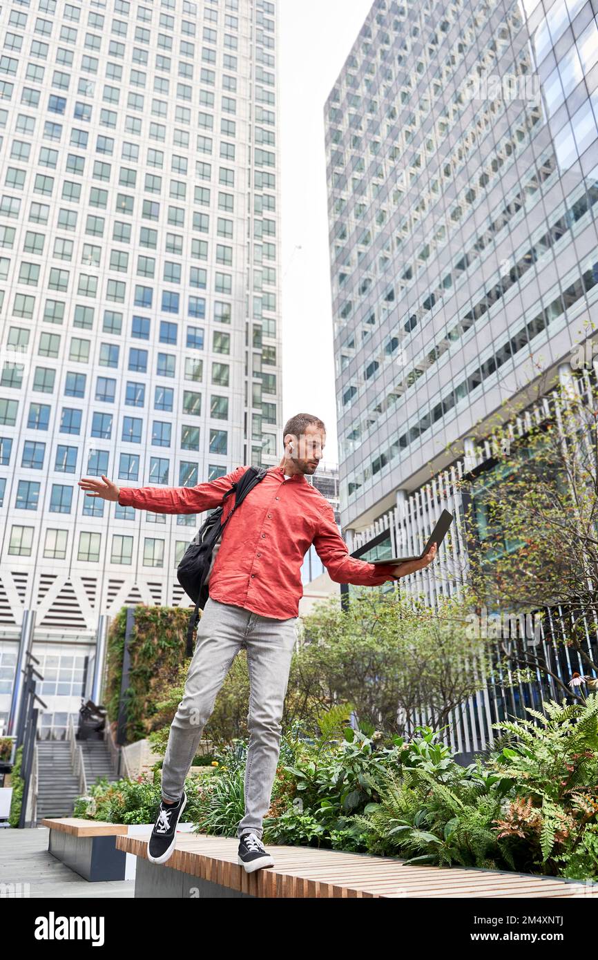 Man with laptop balancing on edge of bench Stock Photo - Alamy