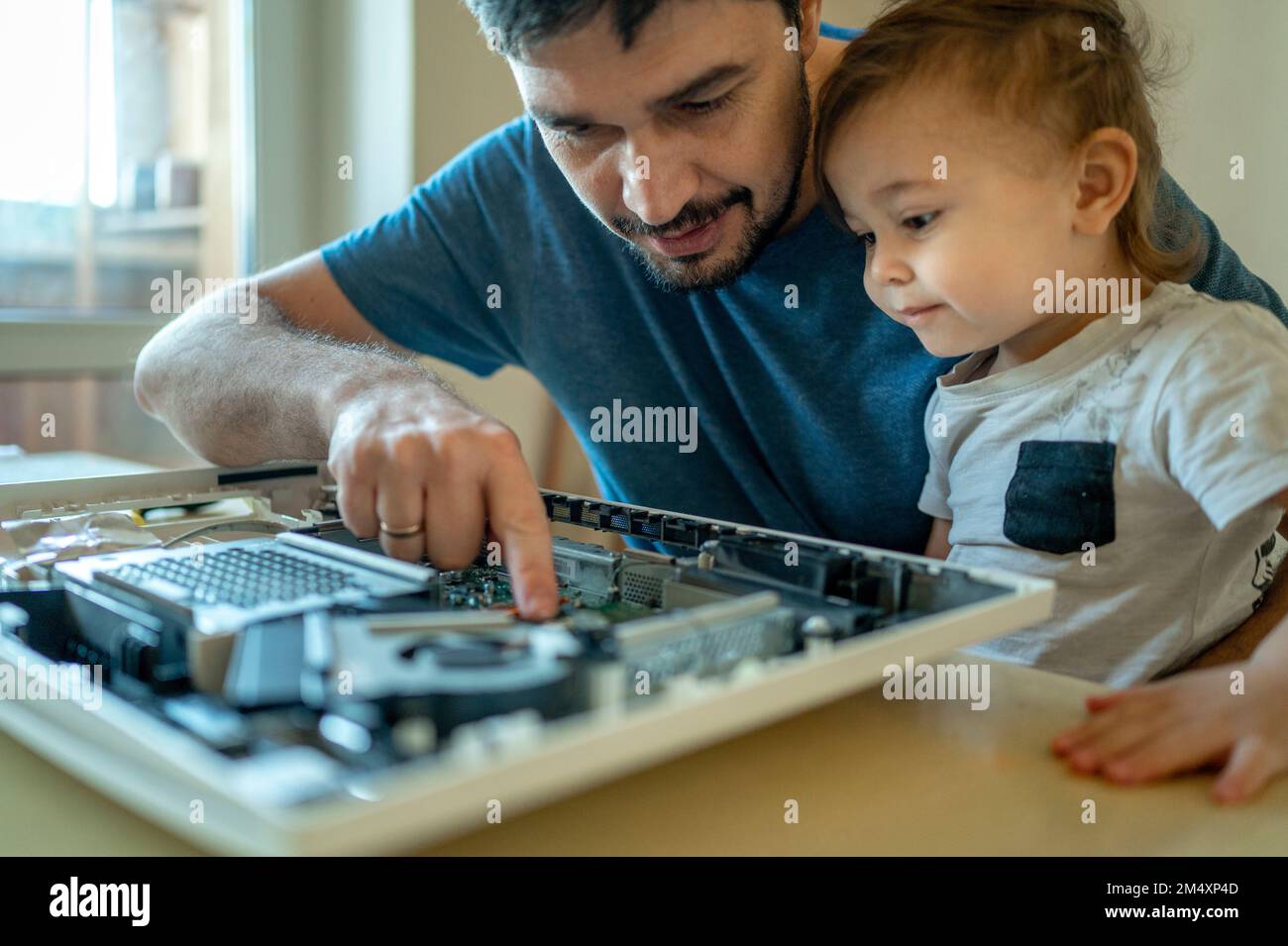 Cute boy looking at father repairing computer on table Stock Photo - Alamy