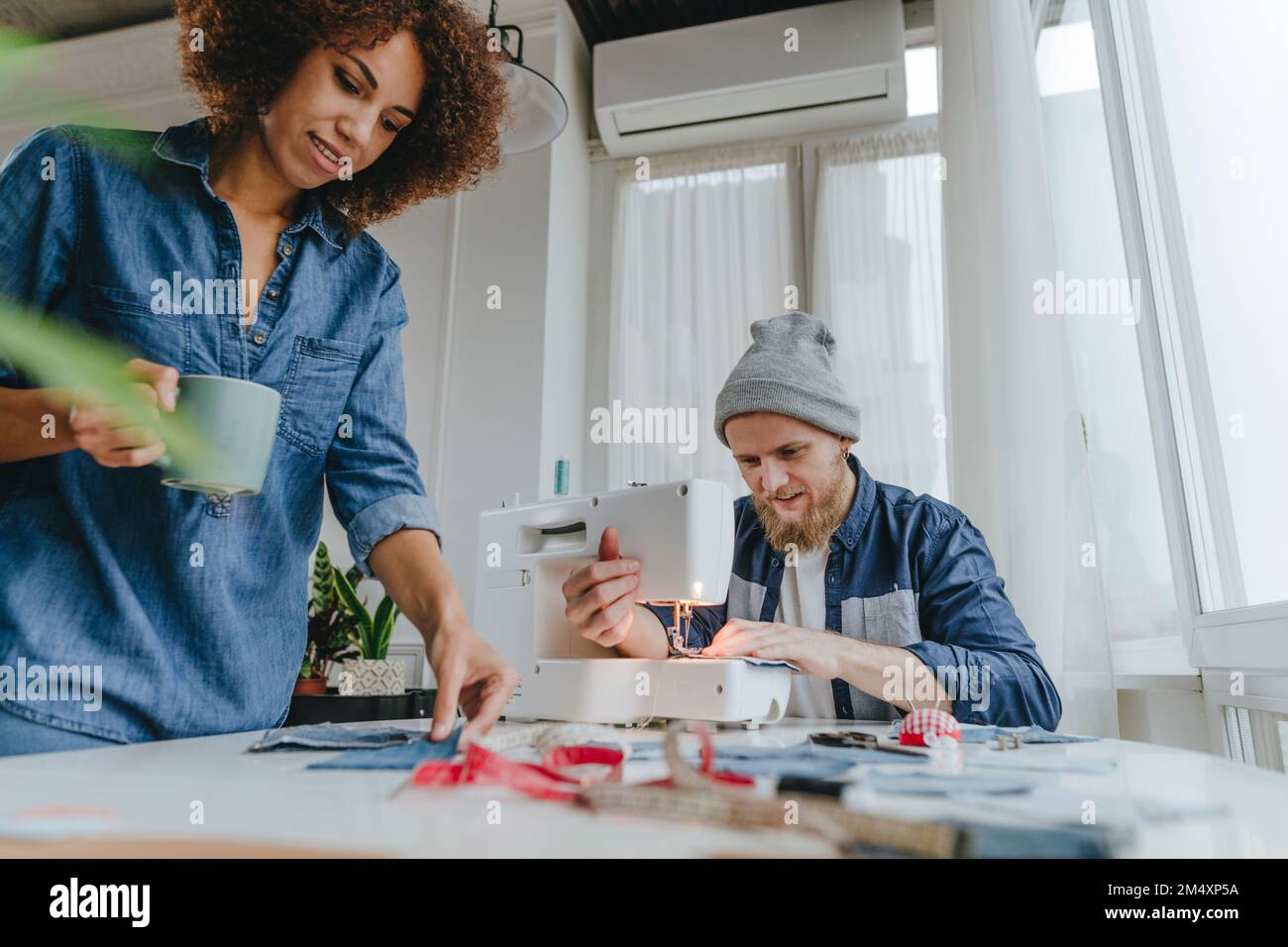 Fashion designer working on sewing machine with colleague examining ...
