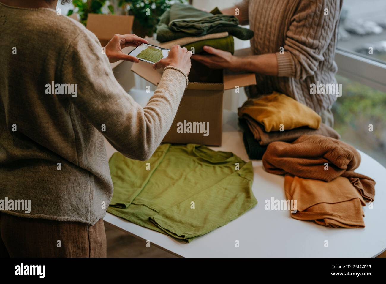 Young fashion designer photographing through smart phone with colleague ...