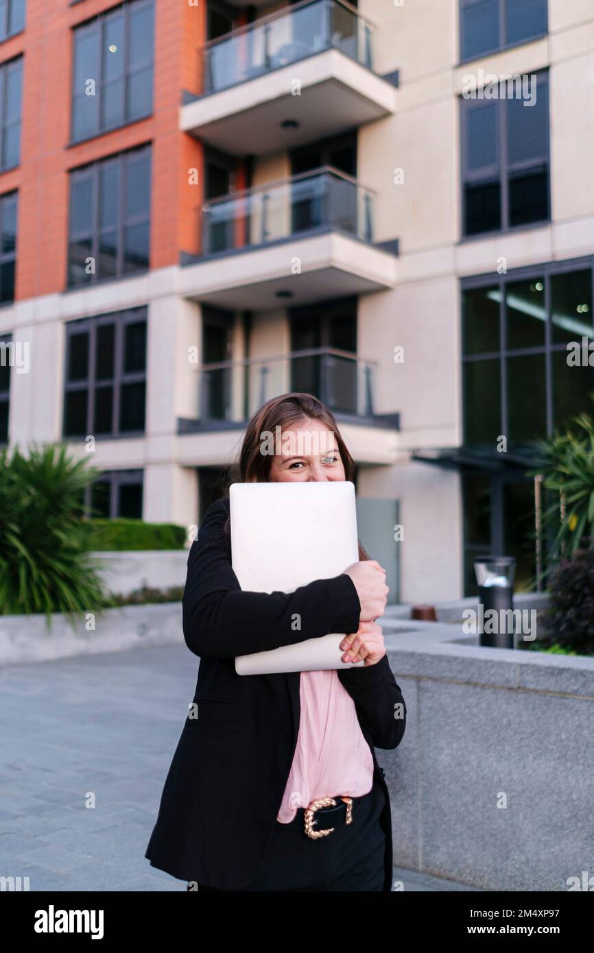 Businesswoman covering face with laptop in front of building Stock ...