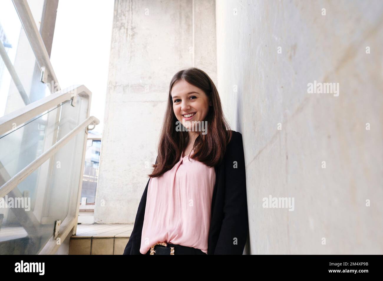 Happy young woman leaning on wall Stock Photo - Alamy