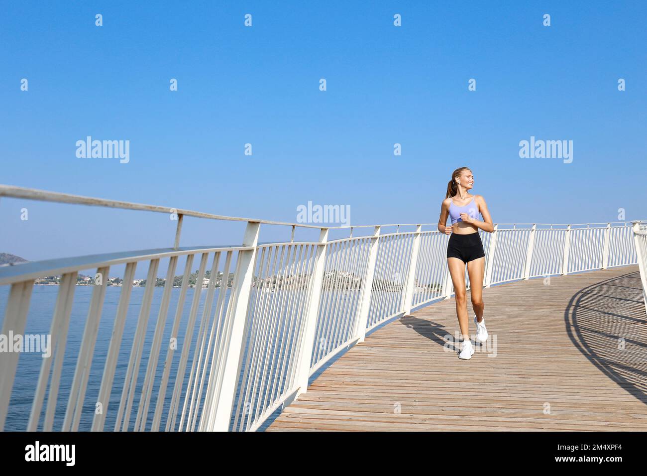 Happy young woman jogging on elevated walkway Stock Photo - Alamy