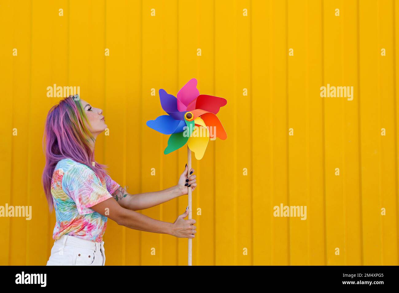 Woman blowing colorful pinwheel toy in front of yellow wall Stock Photo ...