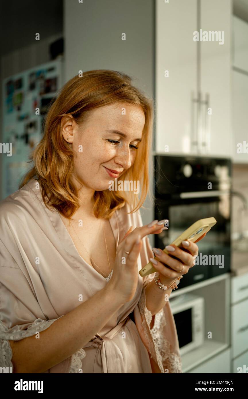 Smiling young woman using smart phone at home Stock Photo - Alamy
