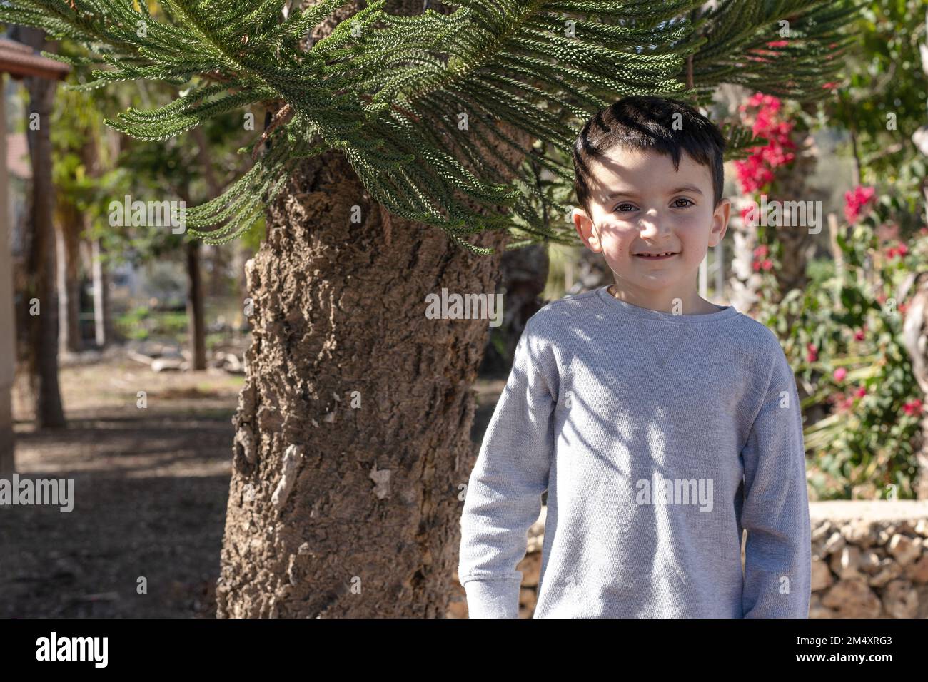 Little happy kid stands in front of tree in springtime and smiling ...