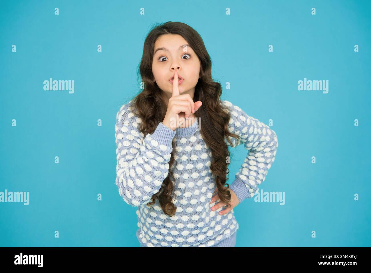 Keep secret. Little girl keep index finger by her lips. Be silent ...