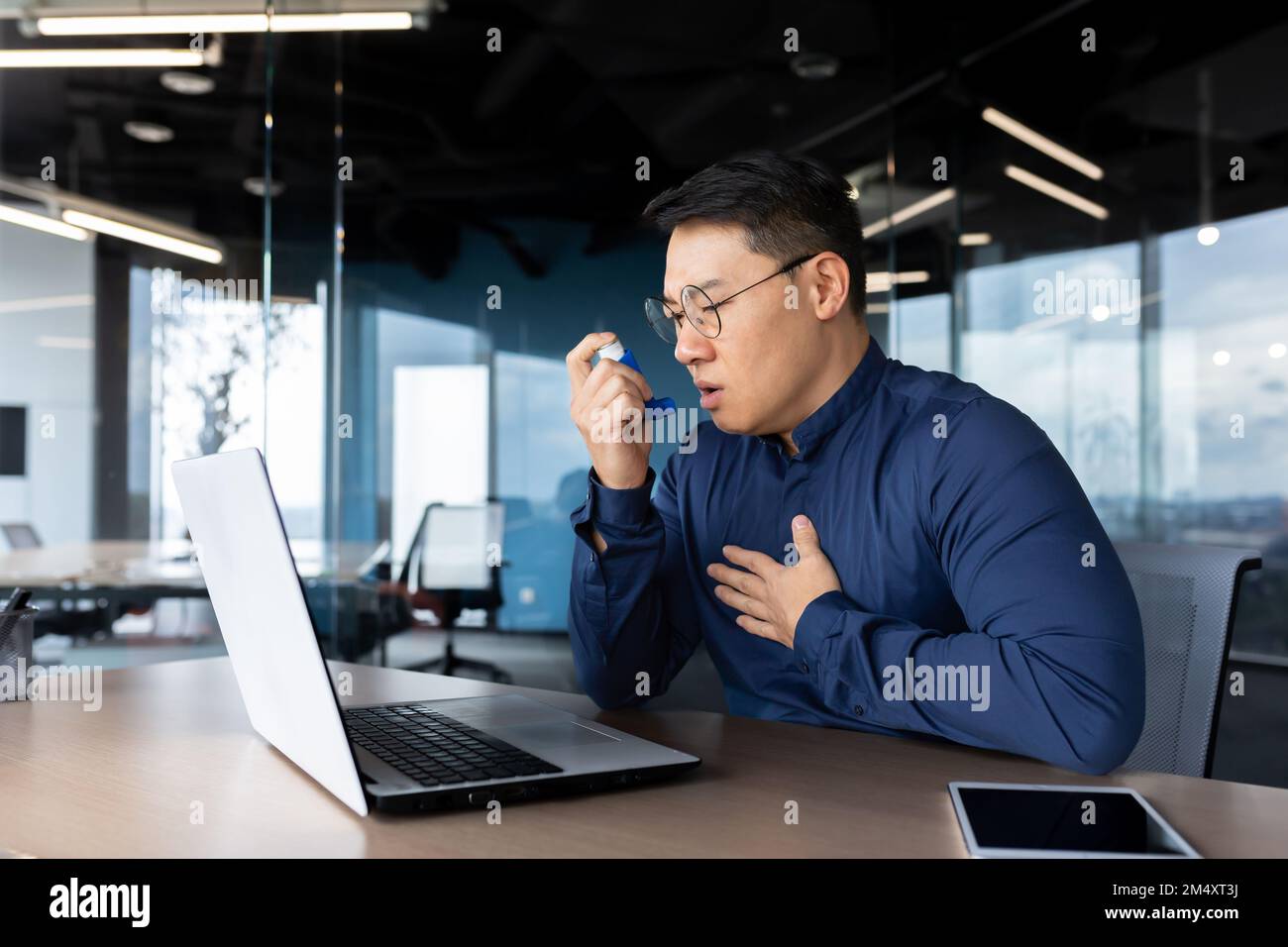 Young male Asian office worker having asthma attack at workplace ...