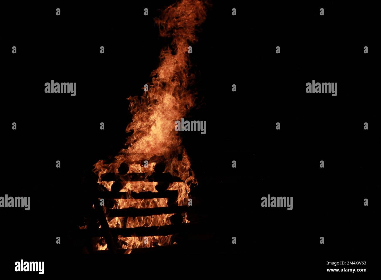 A closeup shot of a burning wood logs bonfire, stacked crosswise on top ...