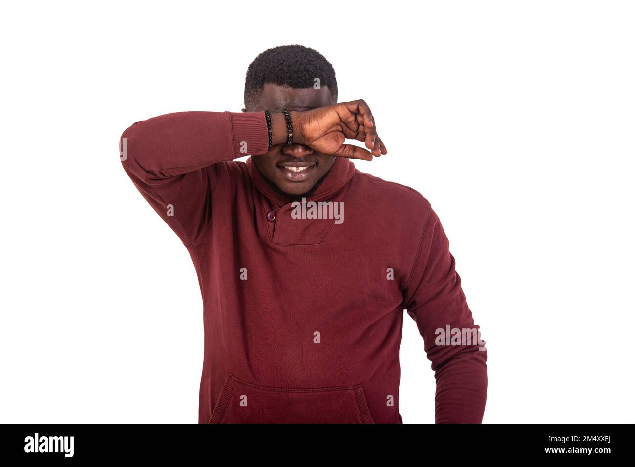 portrait of a handsome young man covering eyes with arm while smiling ...