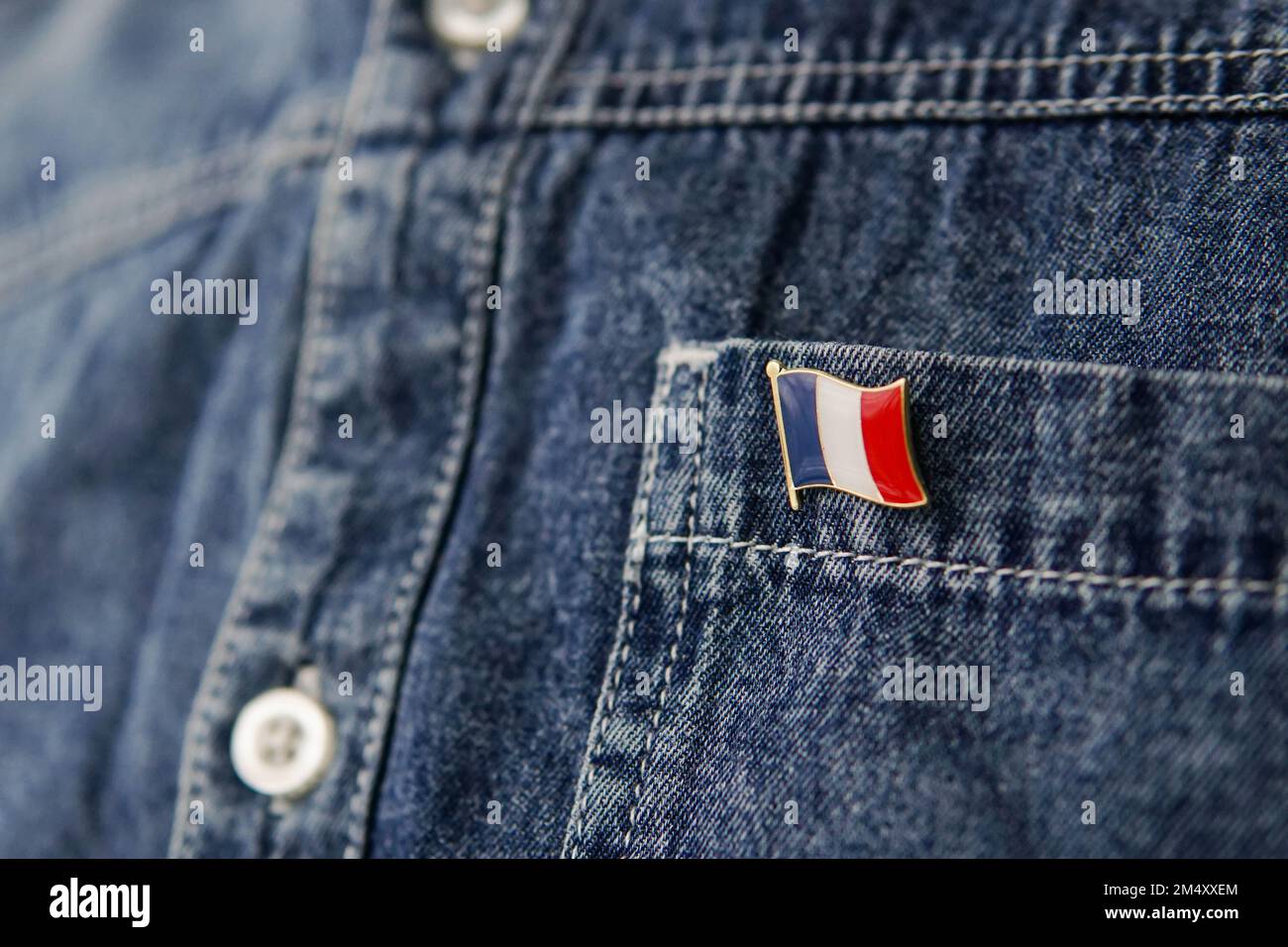 Metal badge with the flag of France is pinned on blue jeans jacket ...