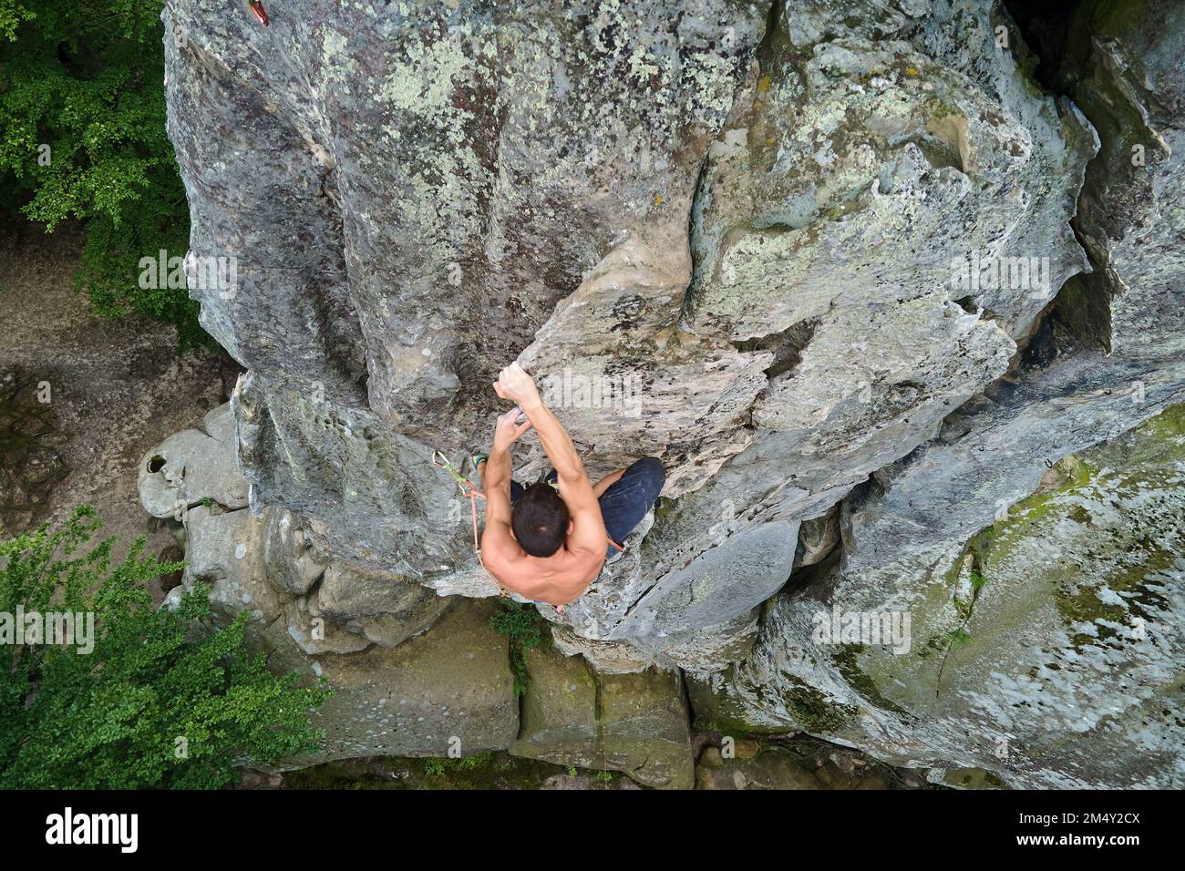 Determined climber clambering up steep wall of rocky mountain ...
