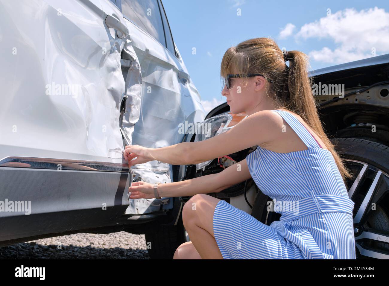 Sad young woman driver sitting near her smashed car looking shocked on ...