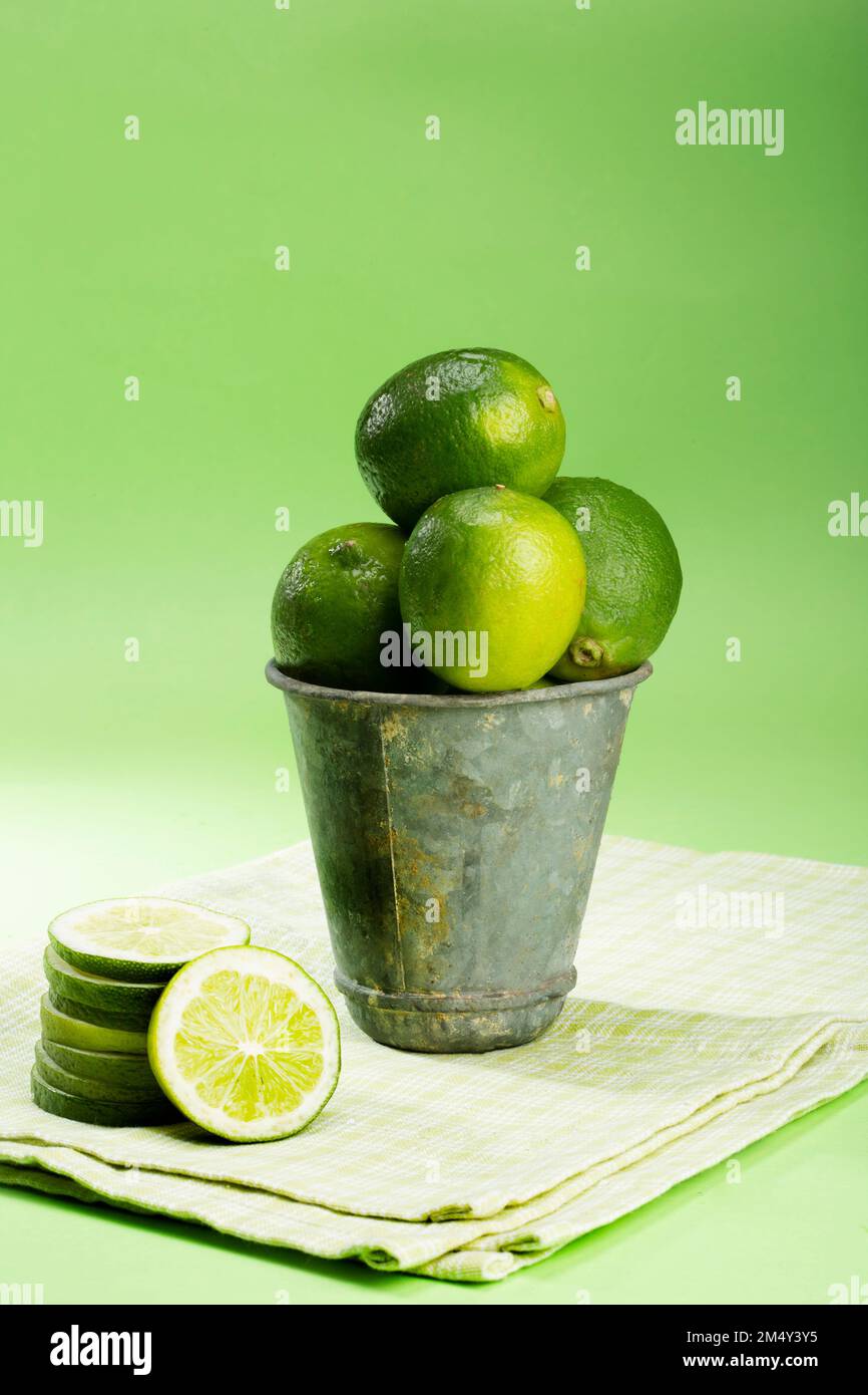 A vertical shot of fresh limes in a meal container on green background ...
