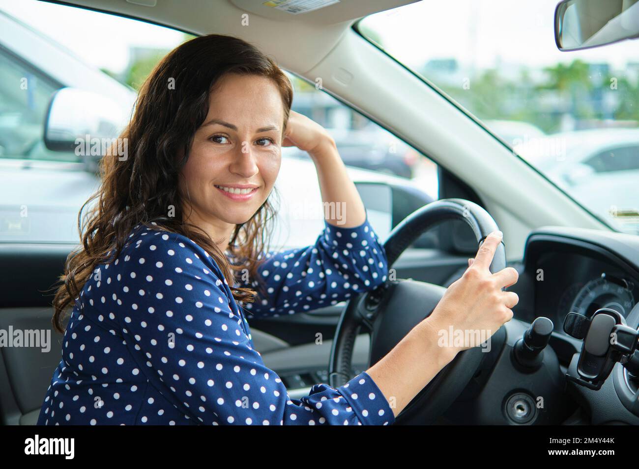 Young stylish woman driver sitting behind steering wheel of her car ...