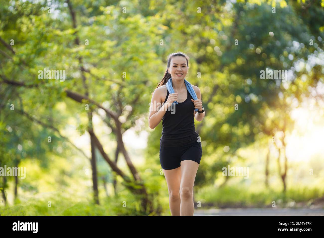 A fit Asian female jogging in a park in black sportswear surrounded by ...