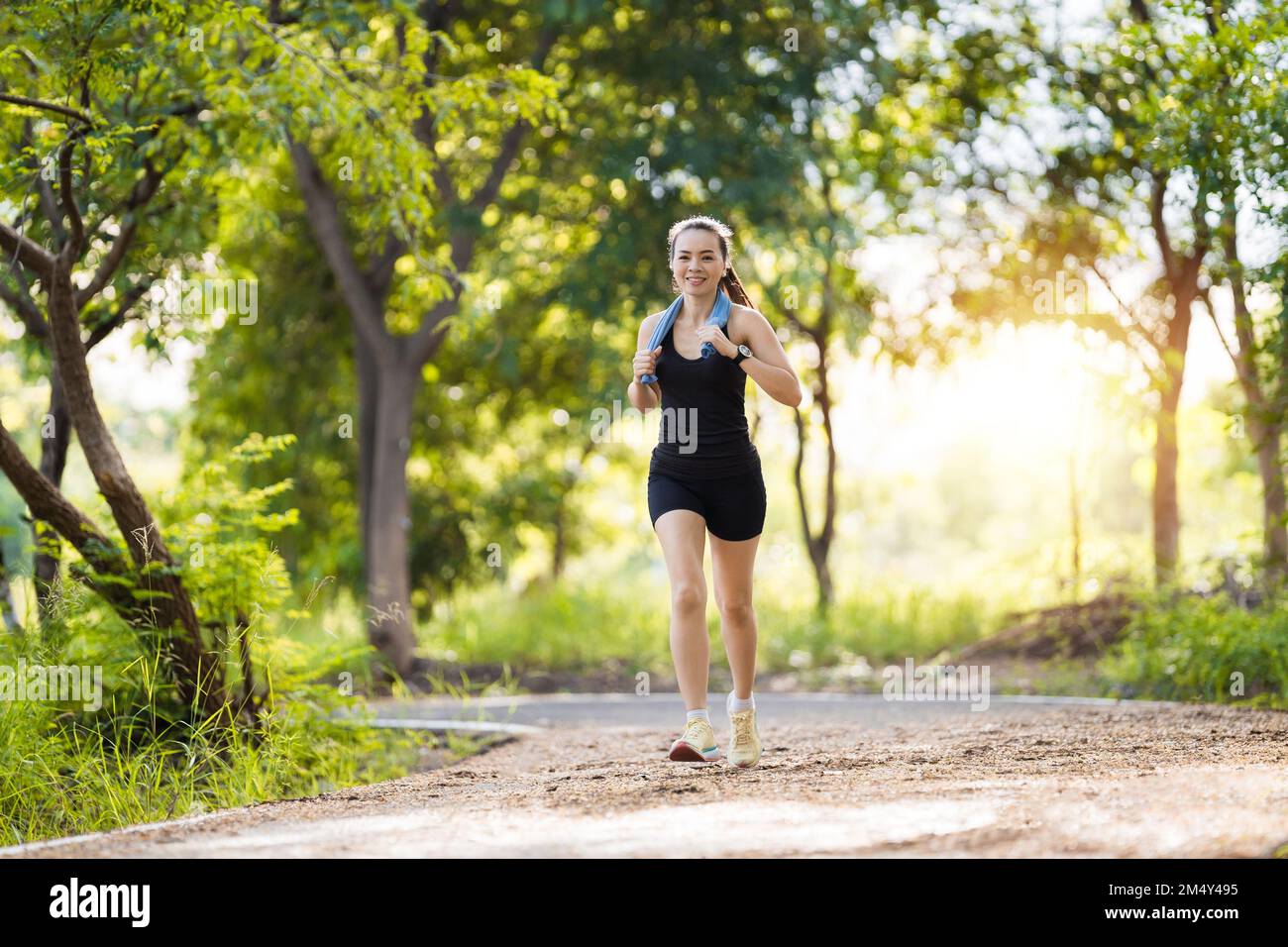 A fit Asian female jogging in a park in black sportswear surrounded by ...