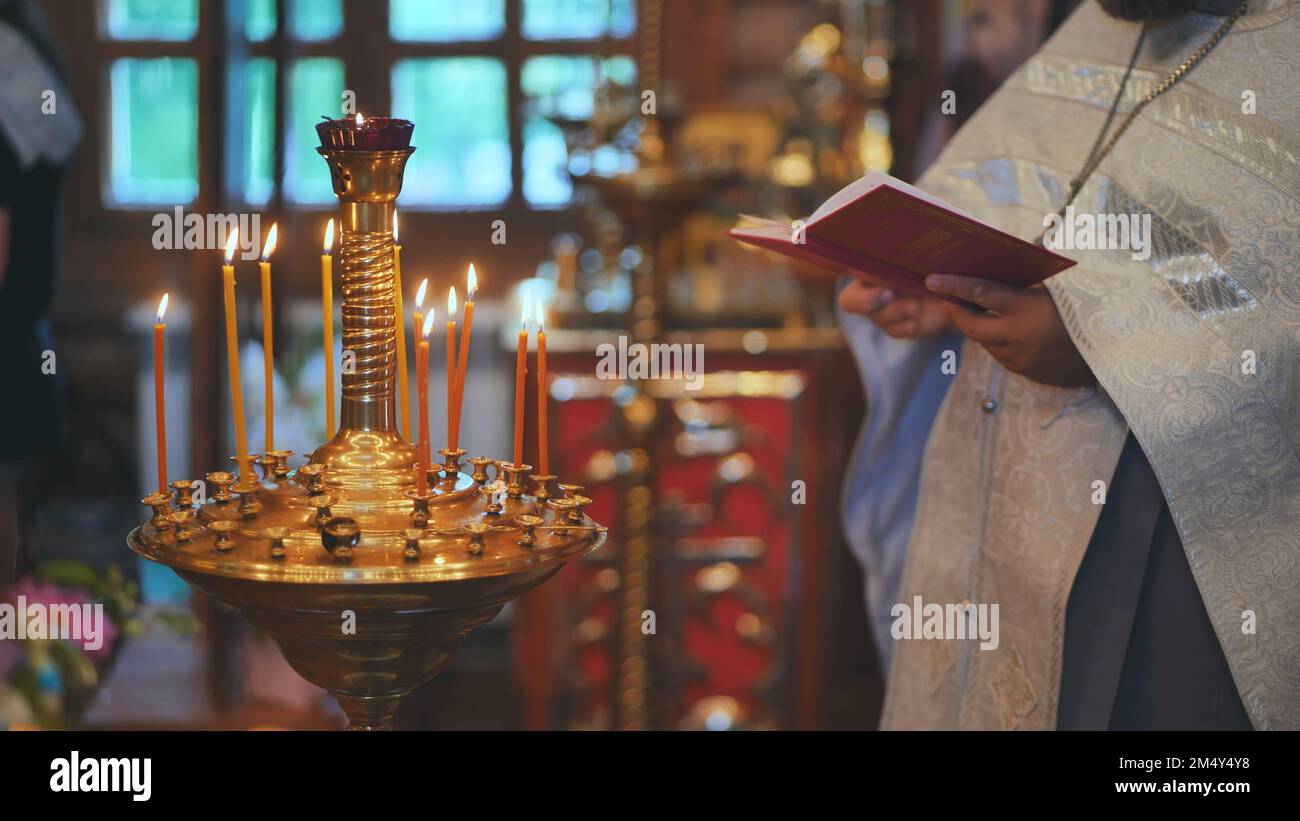 Burning candles against the background of the Priest reading the Bible ...