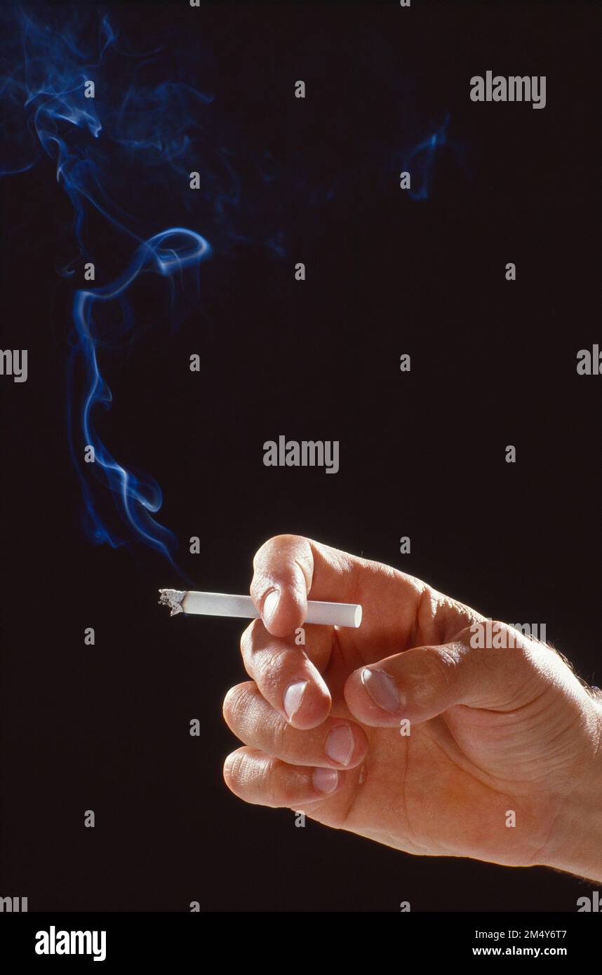 Close-up shot of a hand holding a cigarette smoke is billowing away ...