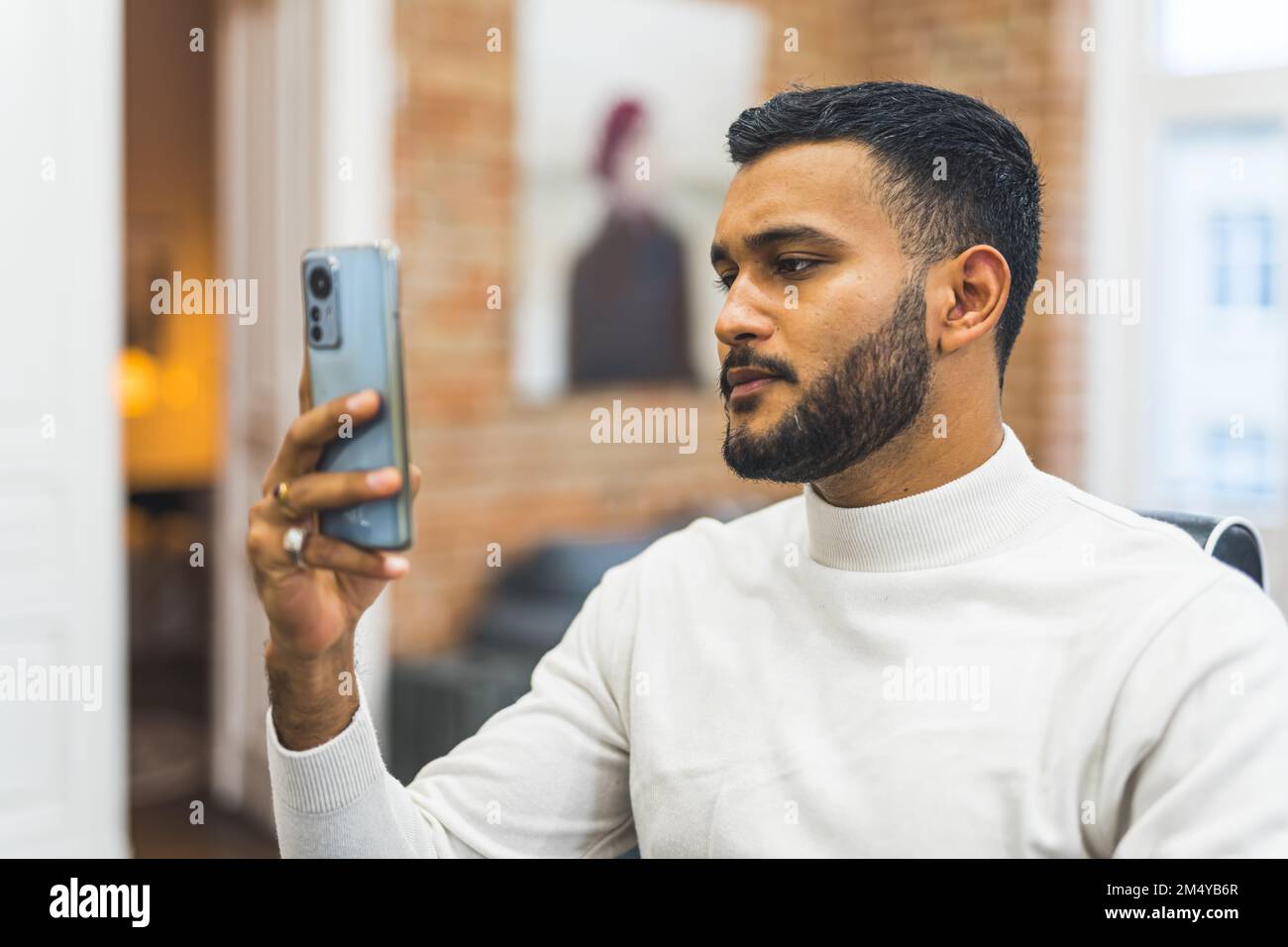 Well-groomed Indian man holding his phone on the eye level and sadly ...