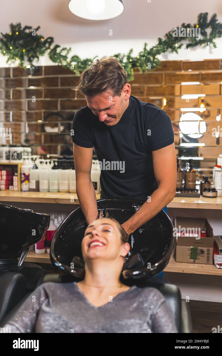 Focused male hairstylist washing hair and massaging the scalp of his ...