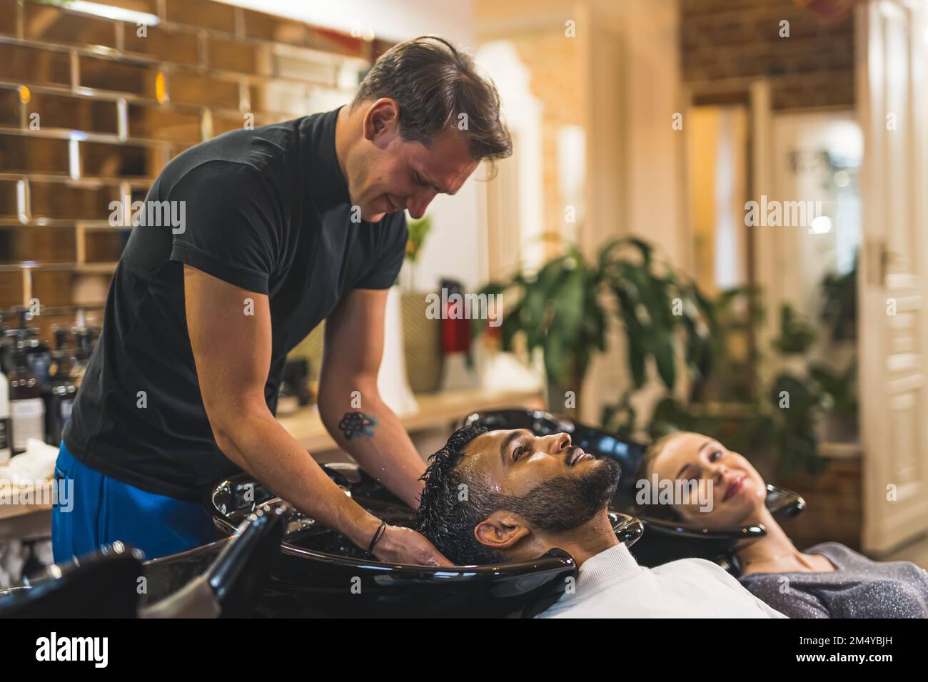 Positive hairstylist man washing his client's black hair. Modern ...
