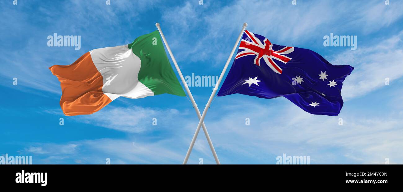 two crossed flags Australia and Ireland waving in wind at cloudy sky ...
