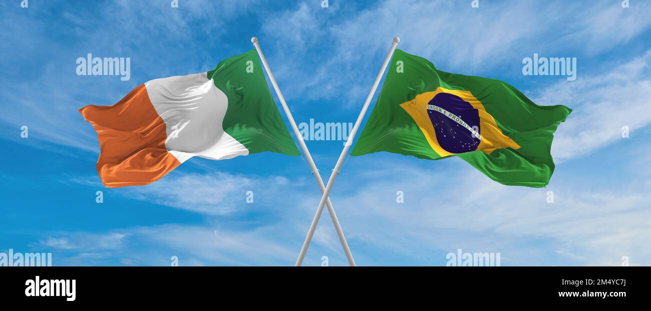 two crossed flags Brazil and Ireland waving in wind at cloudy sky ...