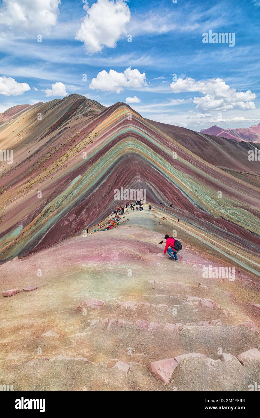 Tourist climbs in the foreground of the Rainbow Mountains at an ...