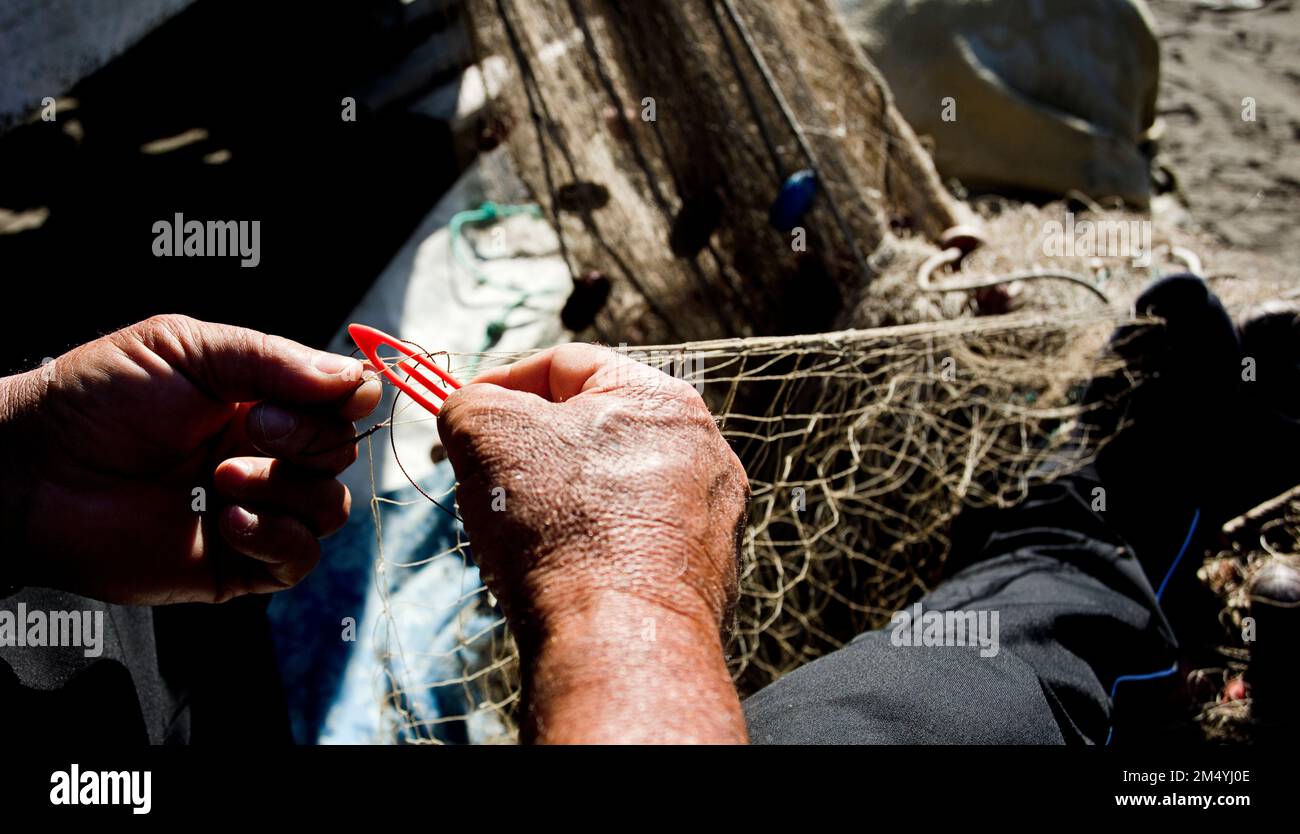 fishing net in the hands of fisherman, he weaves and repairs by sewing ...