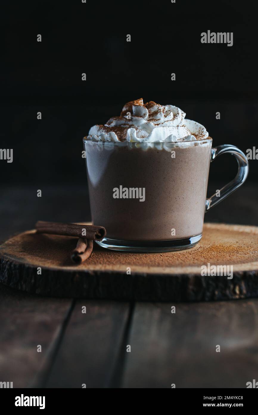 A vertical closeup shot of a glass of hot chocolate on a wooden board ...