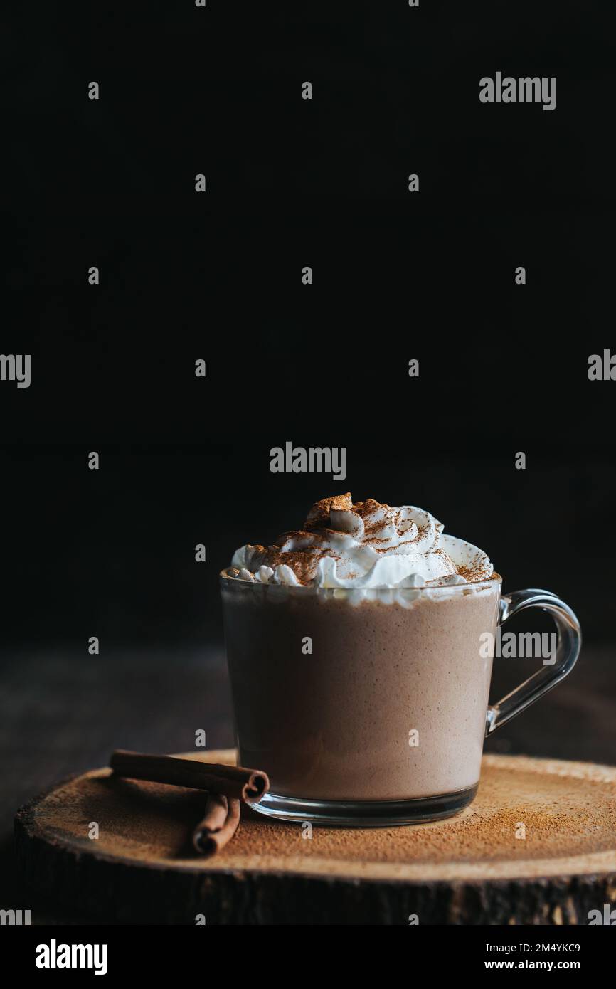 A vertical closeup shot of a glass of hot chocolate on a wooden board ...
