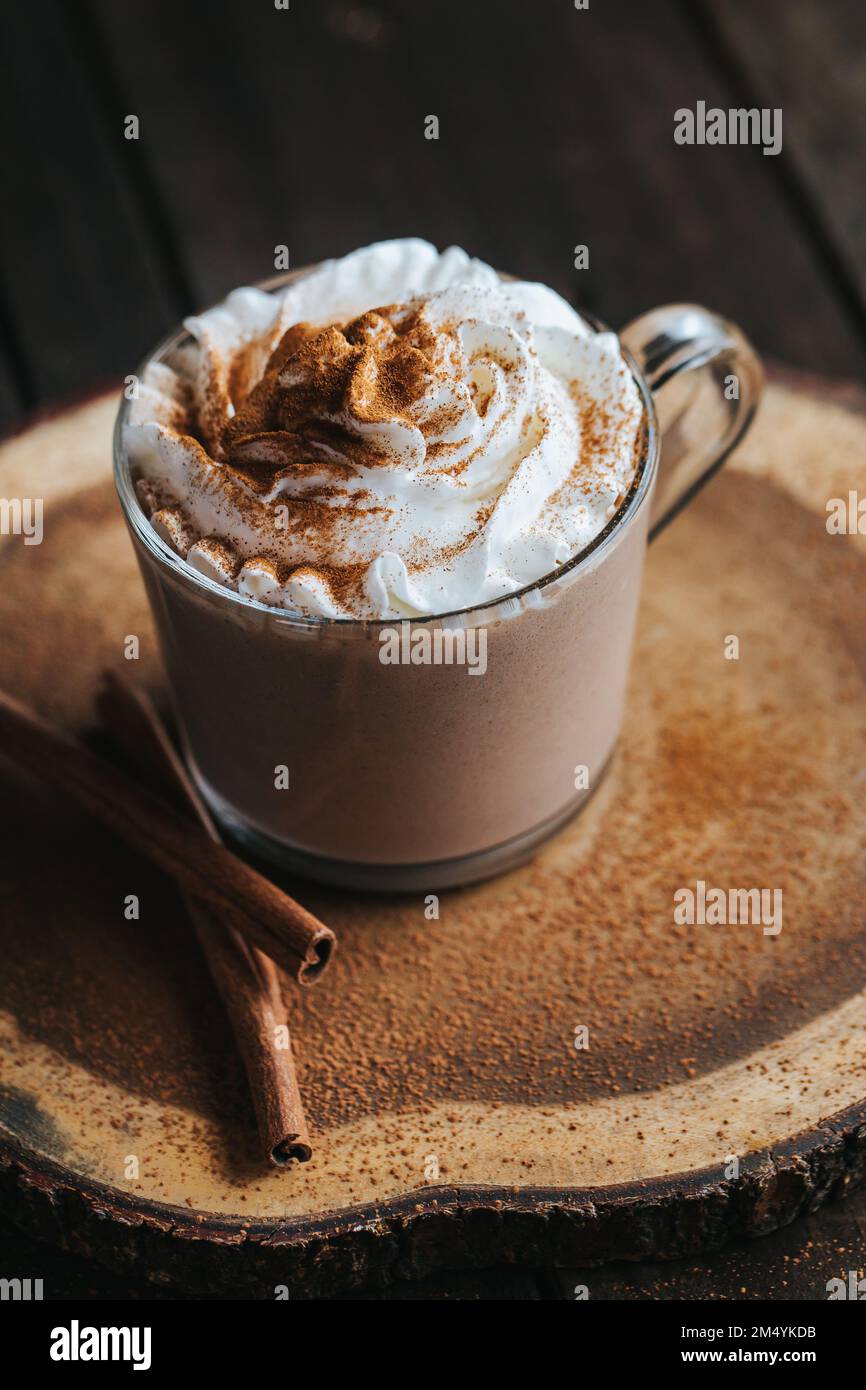 A vertical closeup shot of a glass of hot chocolate on a wooden board ...