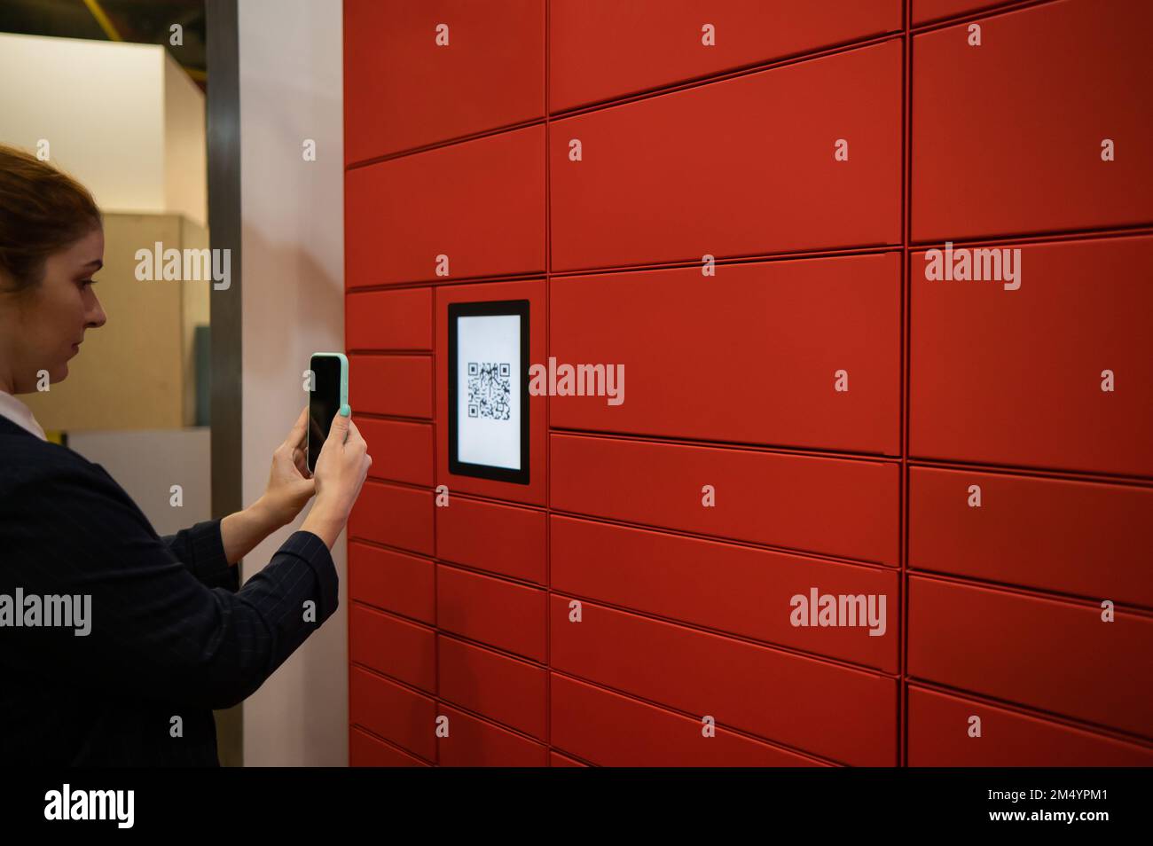 A woman scans a red code to pick up a parcel at a parcel machine ...